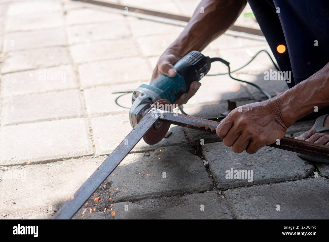 A person using an angle grinder to cut metal on a paved surface ...