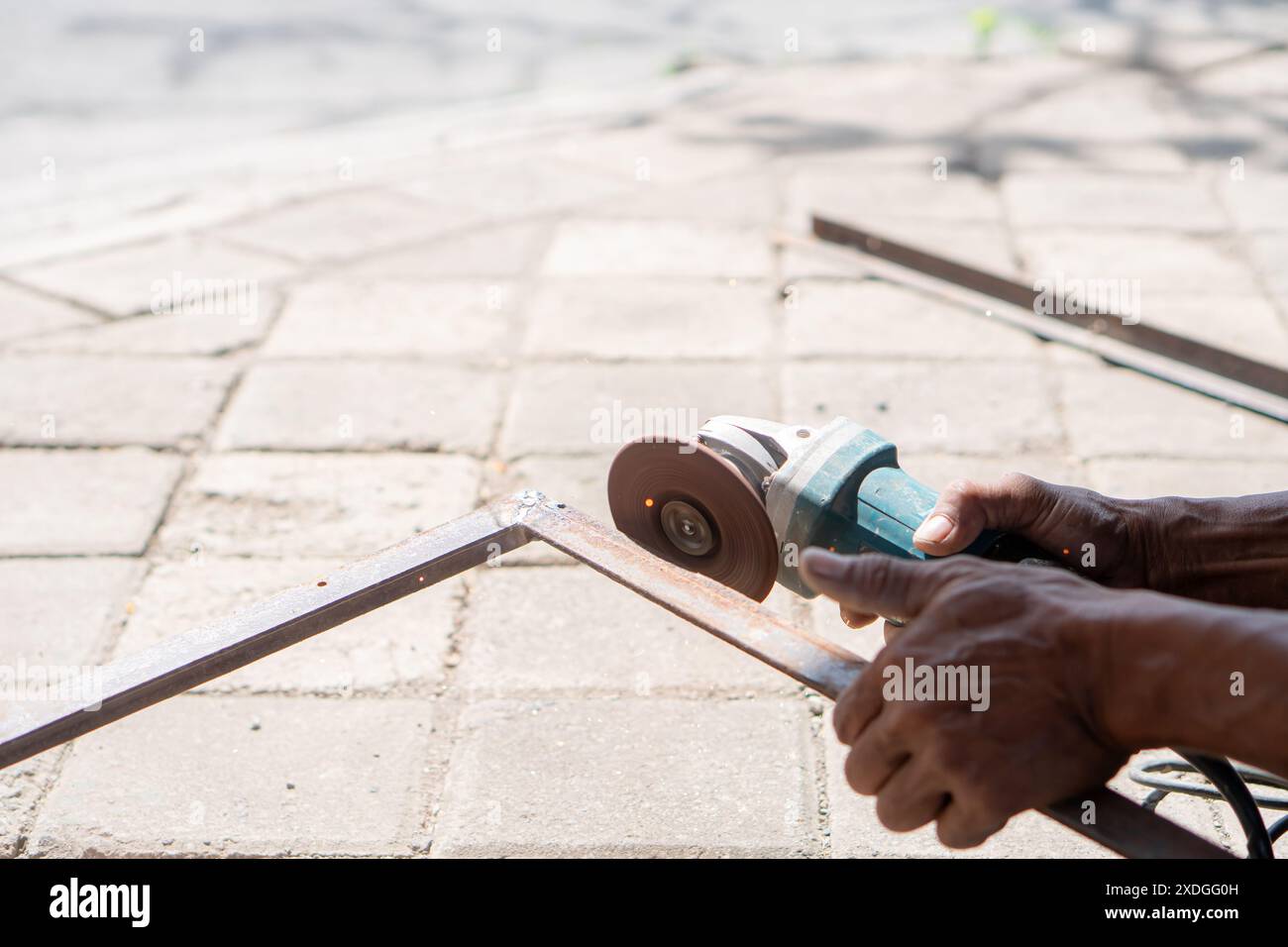 A person using an angle grinder to cut metal on a paved surface ...