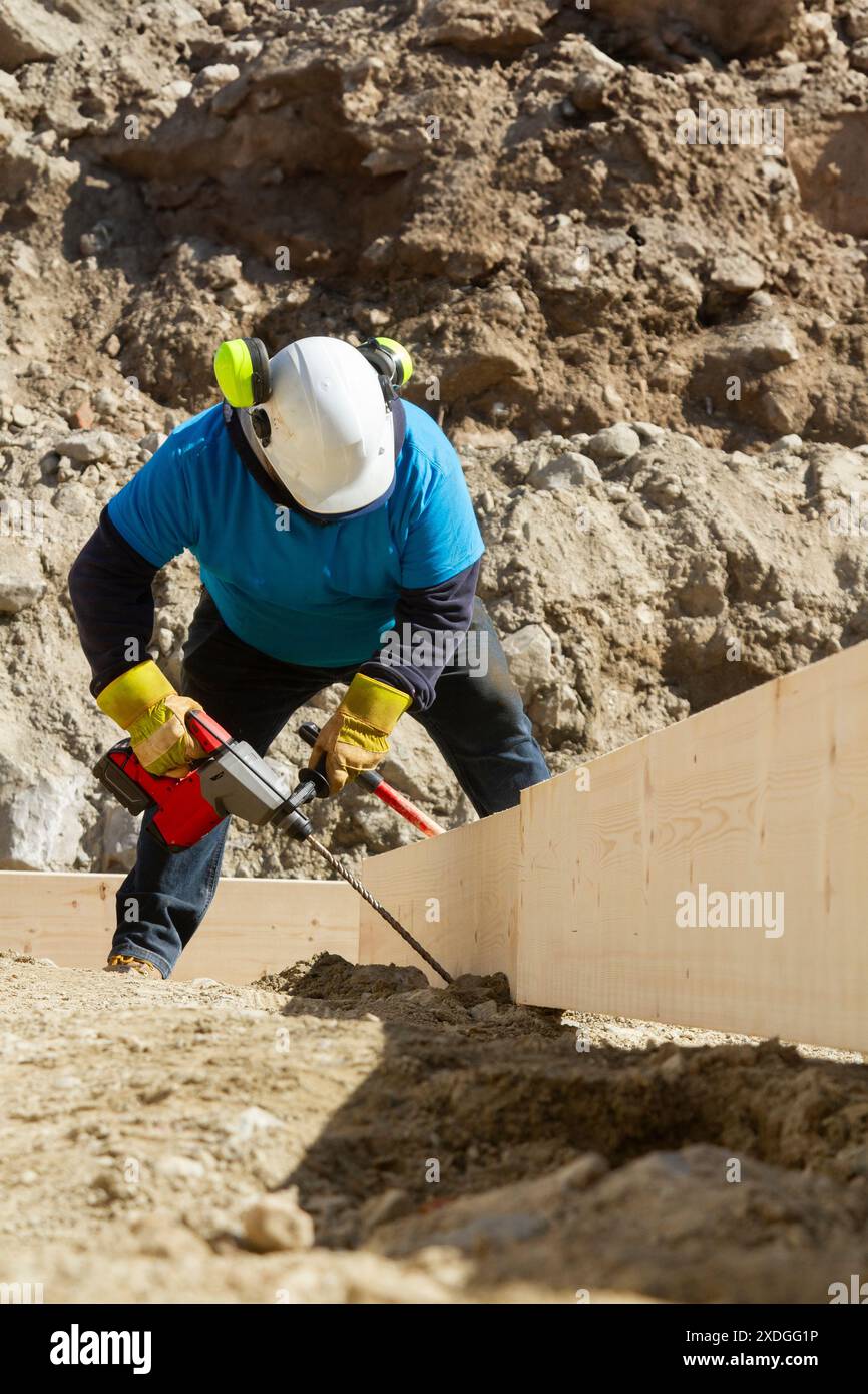 Large, unidentifiable man in blue shirt, white construction hat uses a ...