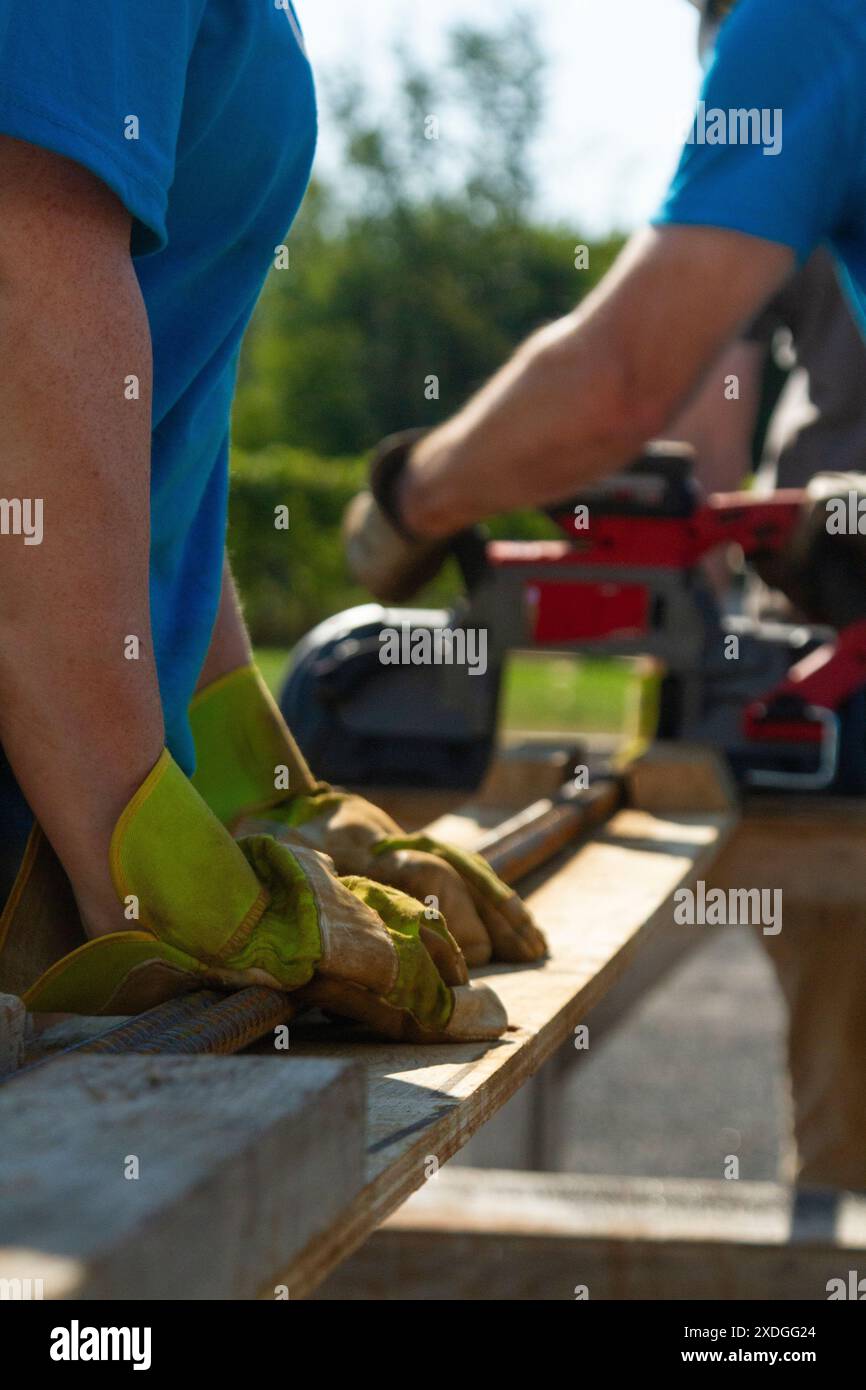 A woman in a blue shirt holds down a piece of rebar while another ...