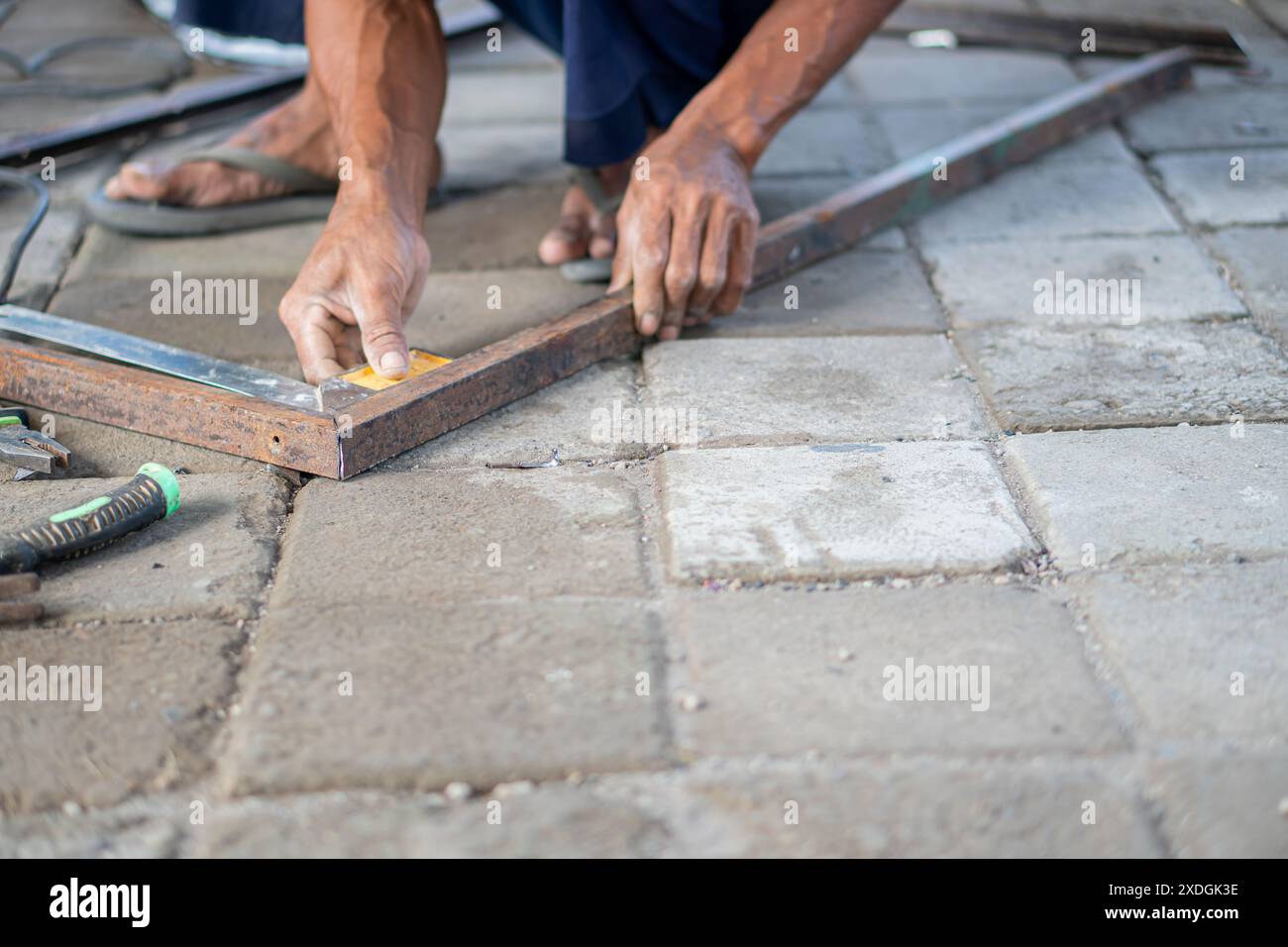 A person measuring a metal frame with a ruler on a paved surface. The ...
