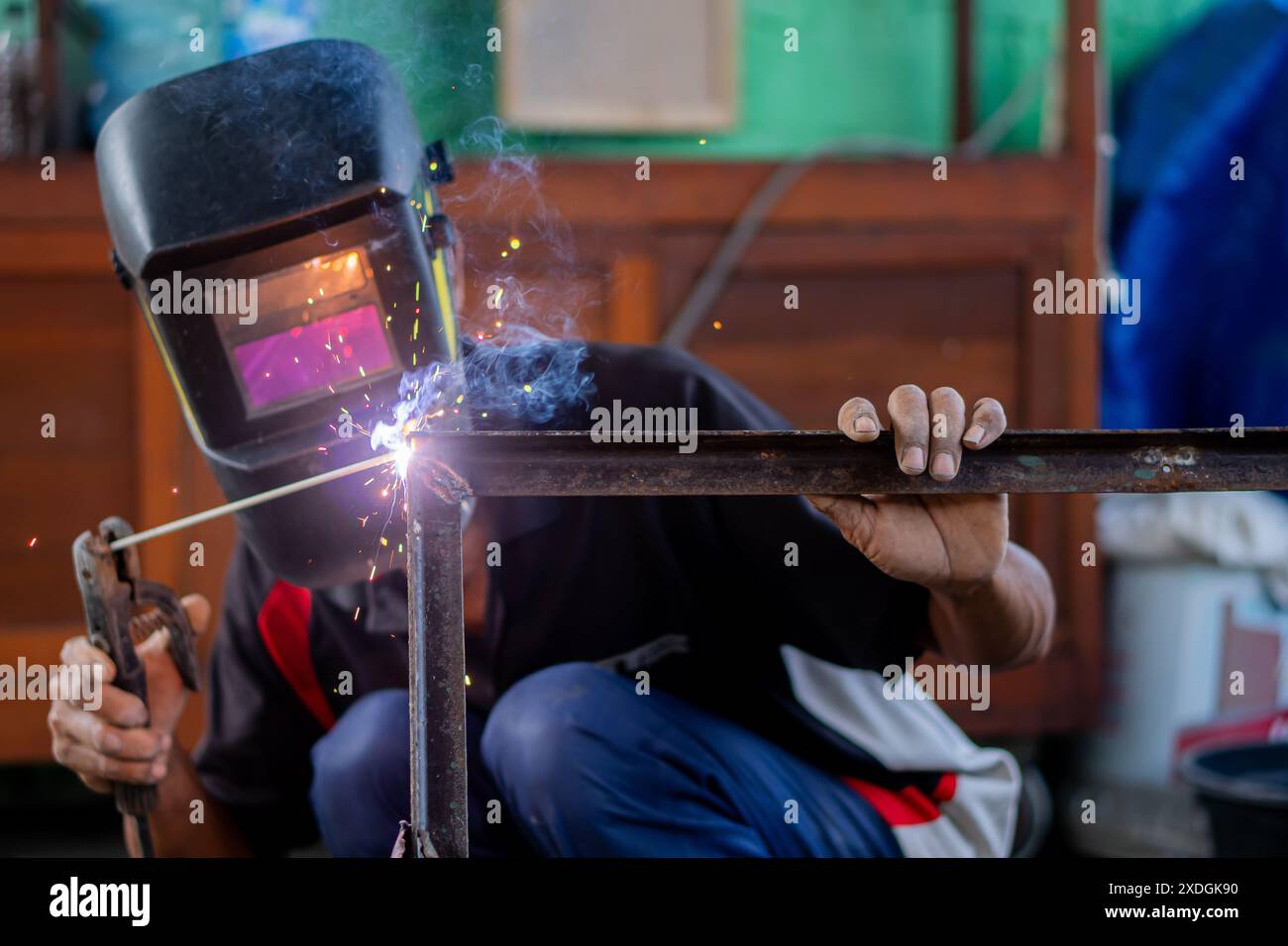 A welder wearing a protective helmet is welding a metal frame, with ...