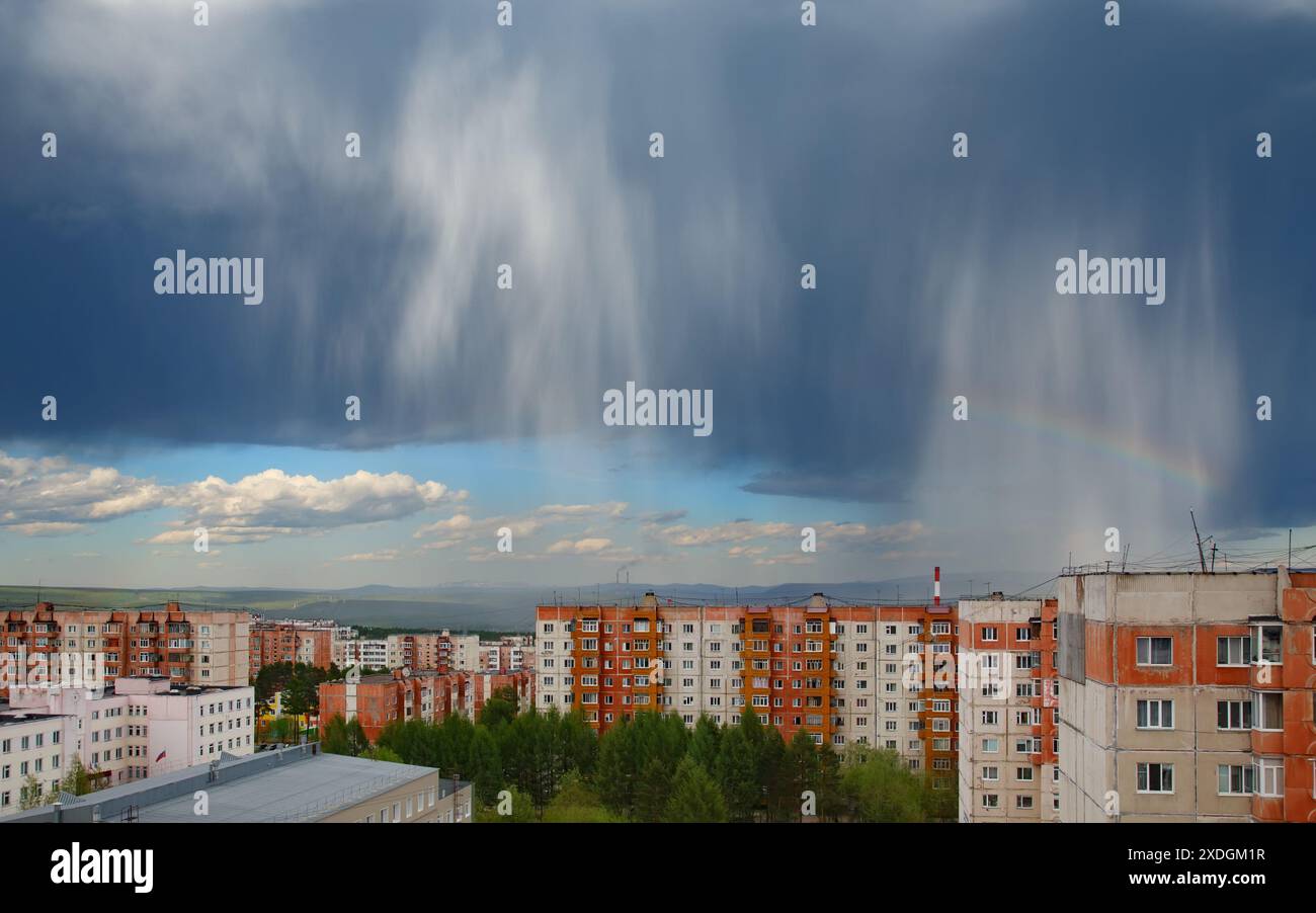 Thunderclouds over the city with a fragment of a rainbow from which ...