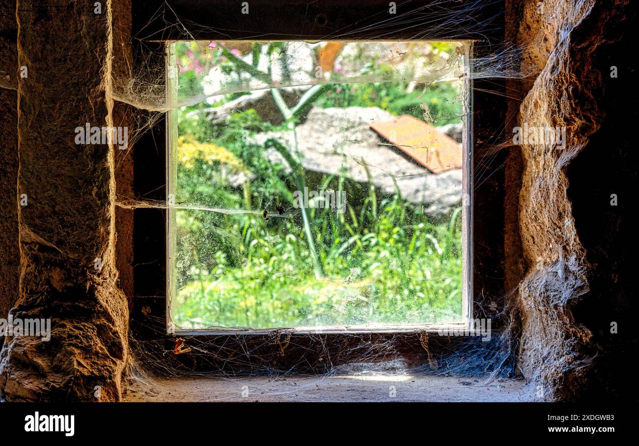 A messy, timeworn, dirty window with a spider web. Inside the church of ...