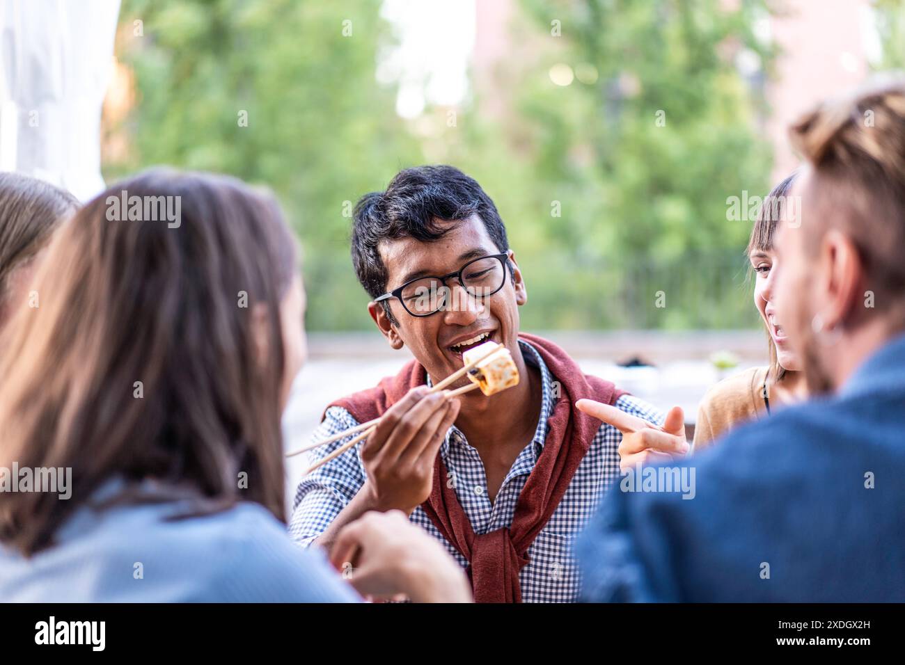 Friends enjoying a meal outdoors with a man about to eat modern sushi ...
