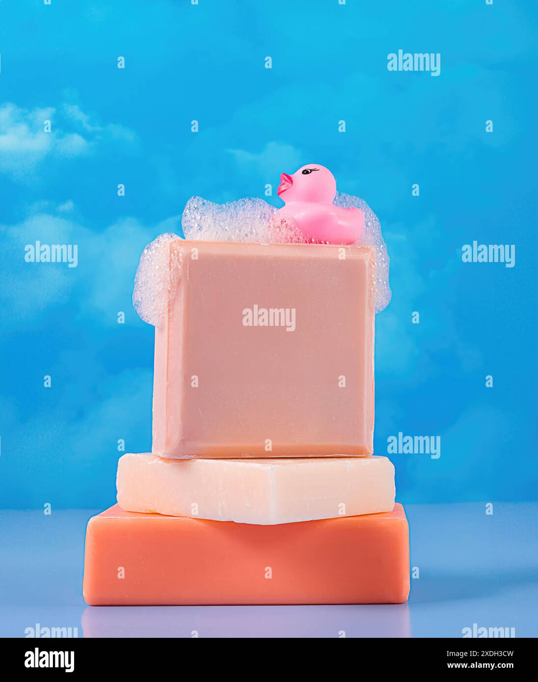 Pink rubber duck on stacked pastel soaps with bubbles, blue sky ...