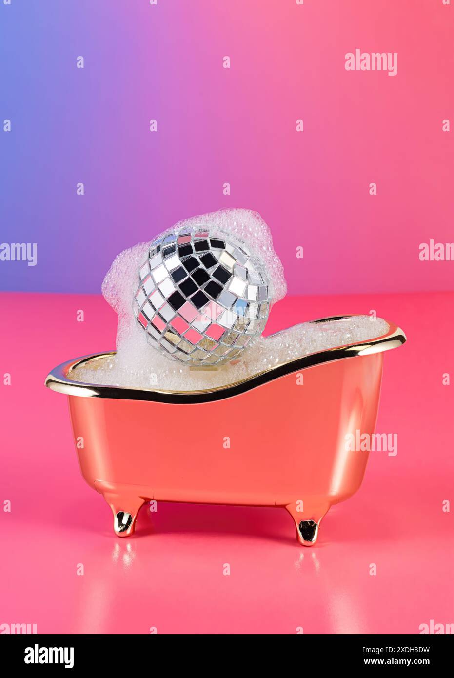 Fashionable disco ball in a bubble-filled gold tub, set against a pink ...