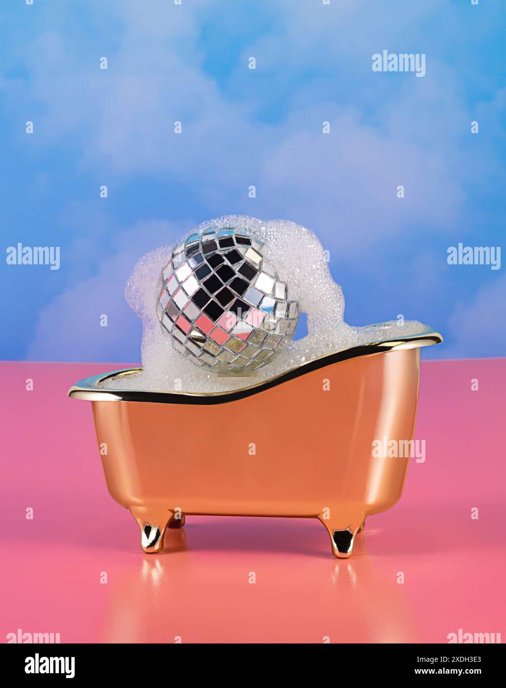 Disco ball in a bubble-filled gold bathtub, blue sky and pink backdrop ...