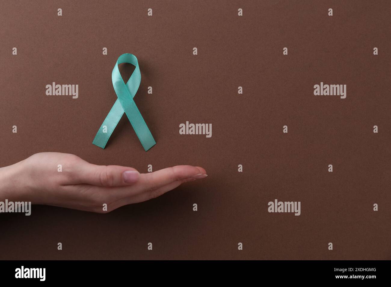 Woman with turquoise awareness ribbon on brown background, top view ...