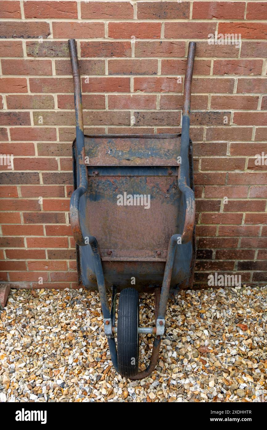 Old rusty wheelbarrow leaning against a red brick wall Stock Photo - Alamy