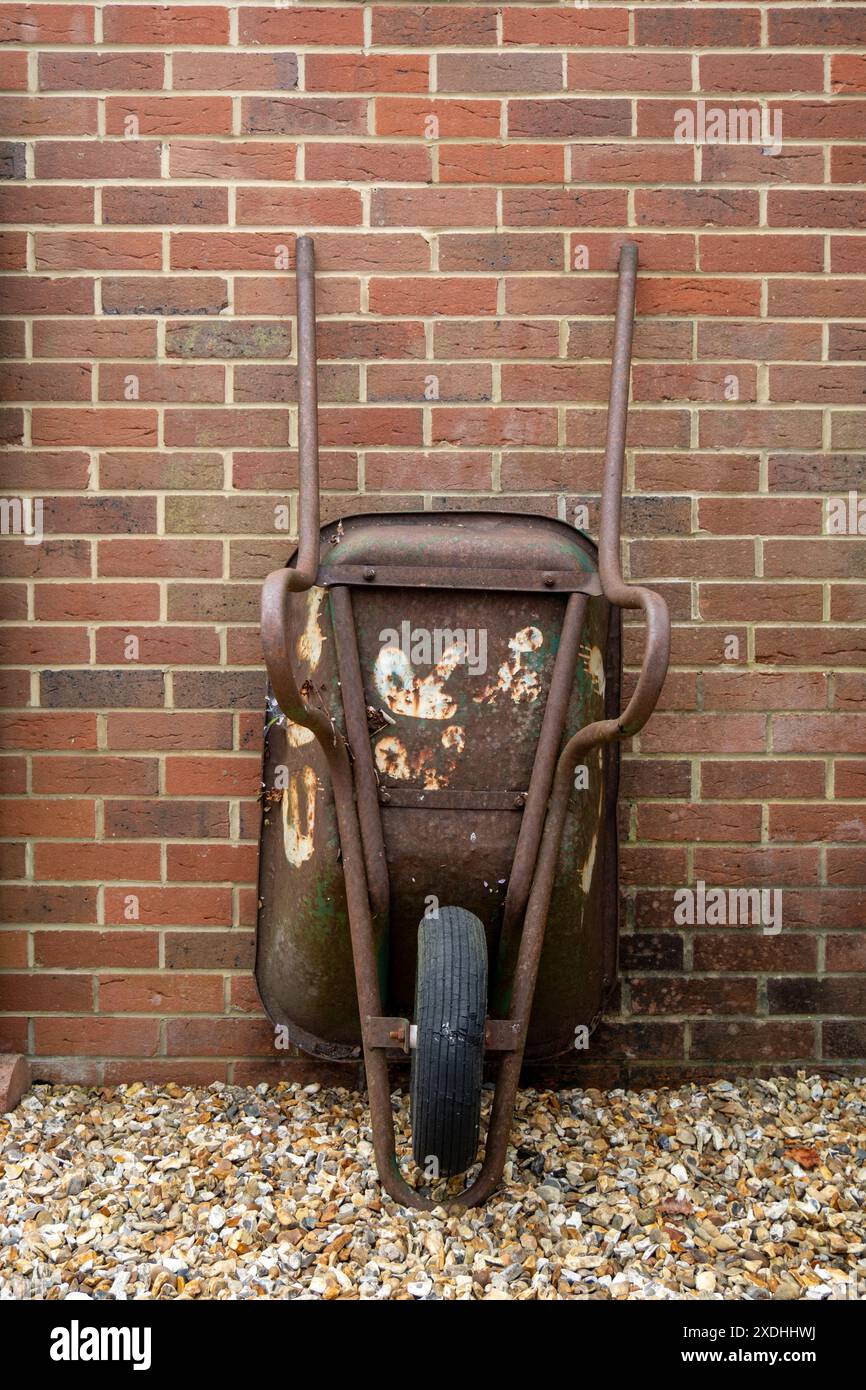 Old rusty wheelbarrow leaning against a red brick wall Stock Photo - Alamy