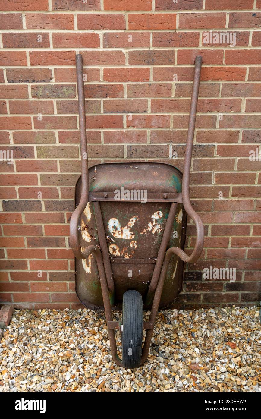 Old rusty wheelbarrow leaning against a red brick wall Stock Photo - Alamy