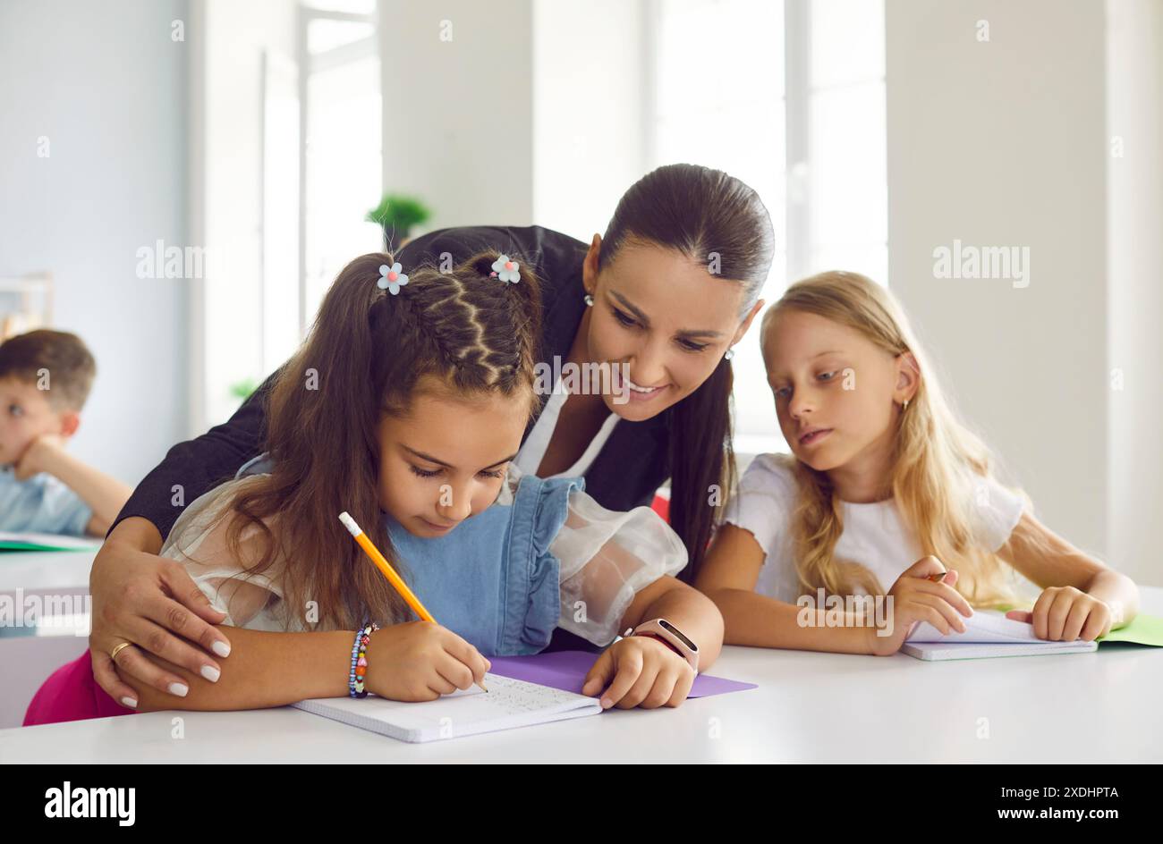Concerned female teacher helping little schoolgirls with lesson in ...