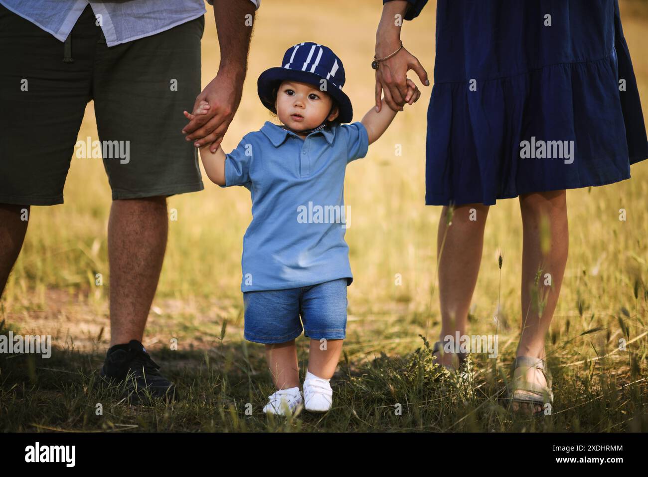A one-year-old boy walking in nature, holding his parents' hands ...