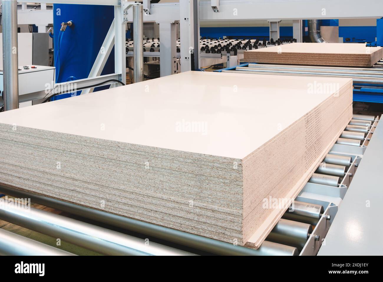 A stack of white boards are being cut by a machine. The boards are all ...