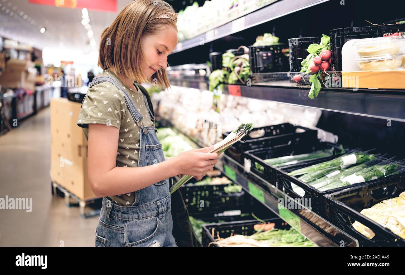 Pretty girl child buying green onion with shopping list in supermarket ...