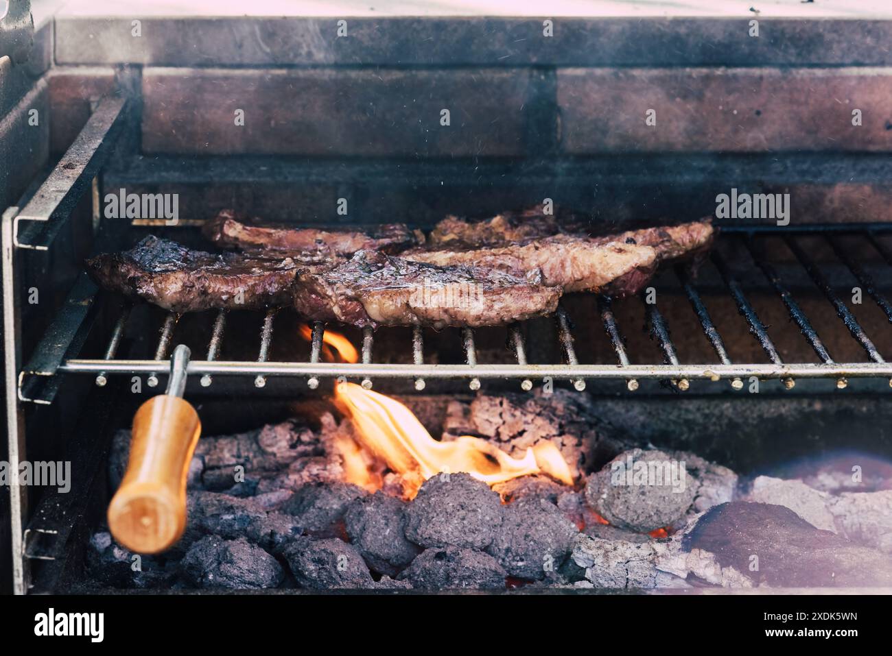 A close-up shot of a grill with three thick pieces of steak cooking over hot coals. The flames ...
