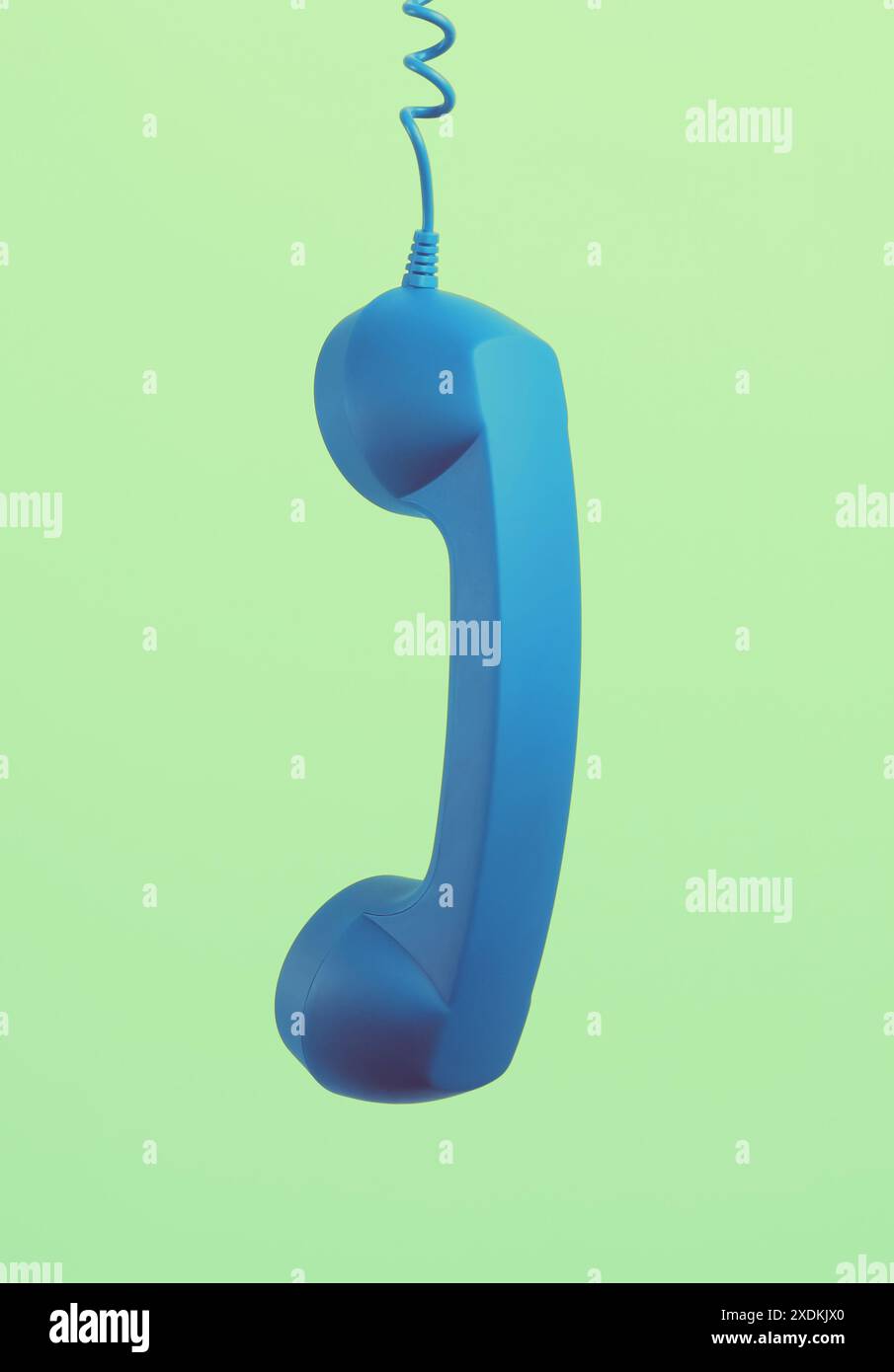 Blue telephone handset hanging on light green background. Space for ...