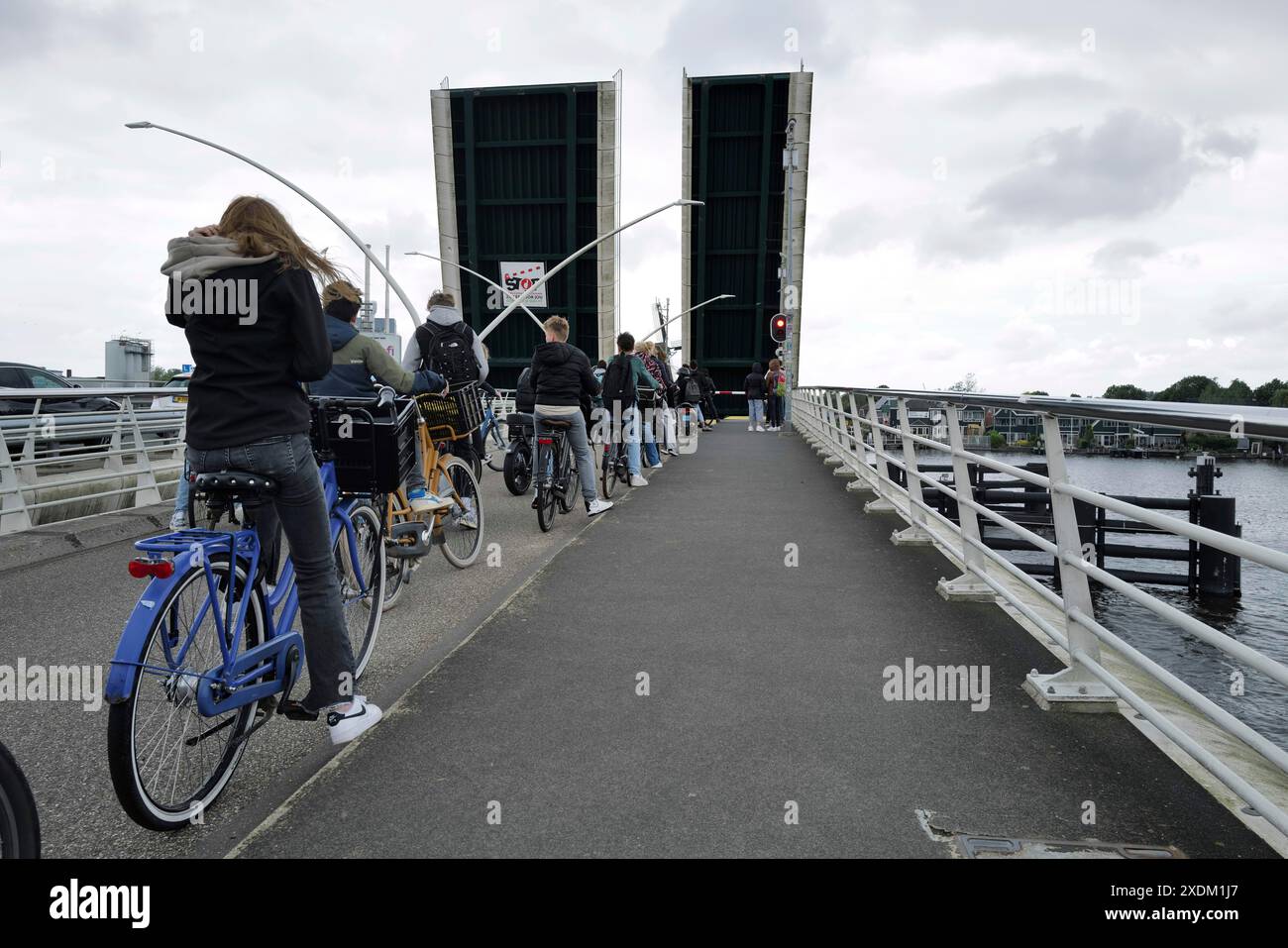 Dutch cyclists without cycling helmets wait on a raised bridge. Zaan ...