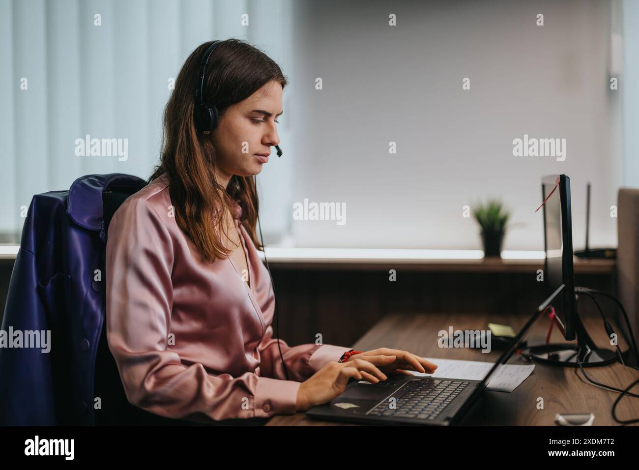 Focused female employee using computer and headset in office setting ...