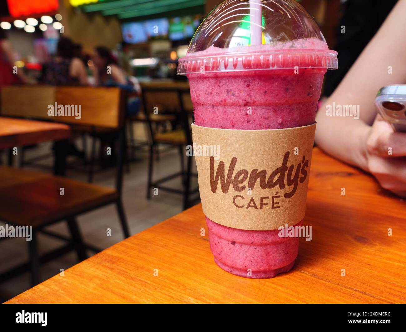 A redberry smoothie in a plastic cup sits on a wooden table in a Wendy's Cafe. The smoothie is ...