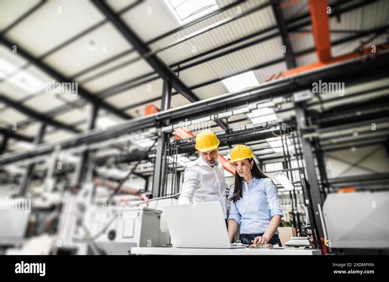 Two project managers standing in modern industrial factory, looking at ...