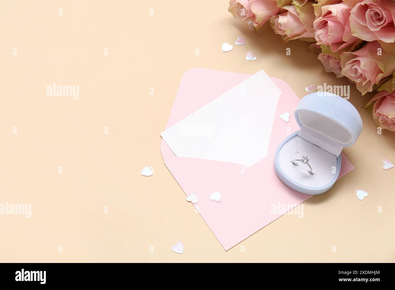 Box with beautiful engagement ring, envelope and pink roses on beige ...