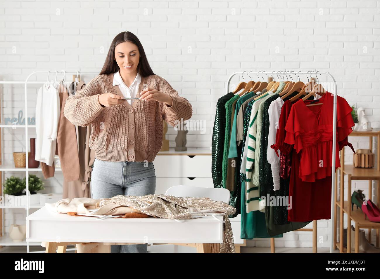 Happy female stylist with clothes on rack taking photo of dress at ...