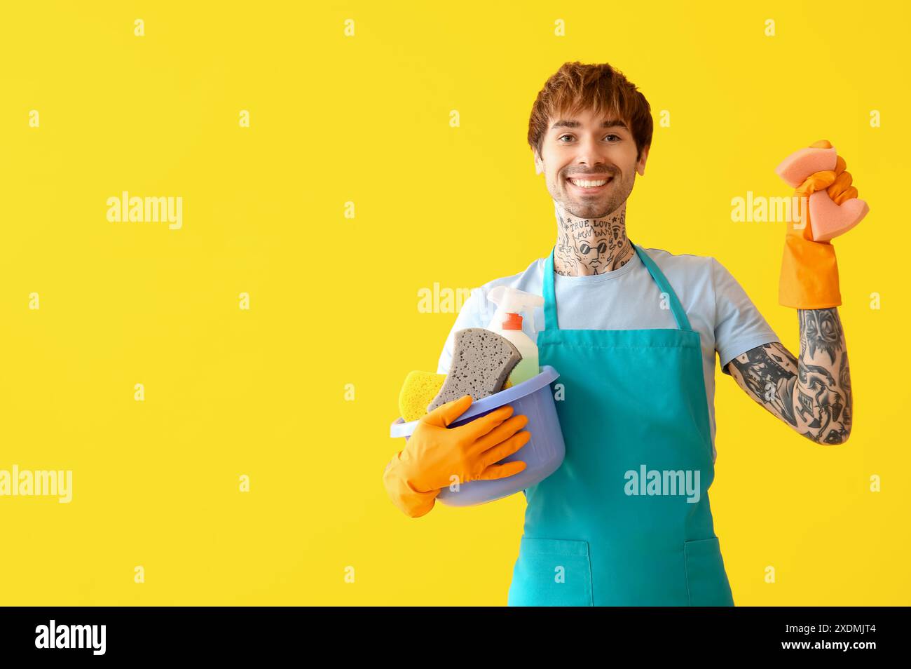 Young tattooed man with cleaning supplies on yellow background Stock ...