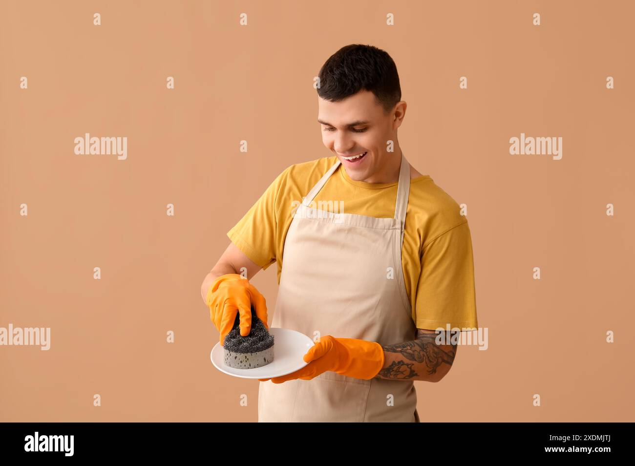 Young tattooed man washing plate on beige background Stock Photo - Alamy