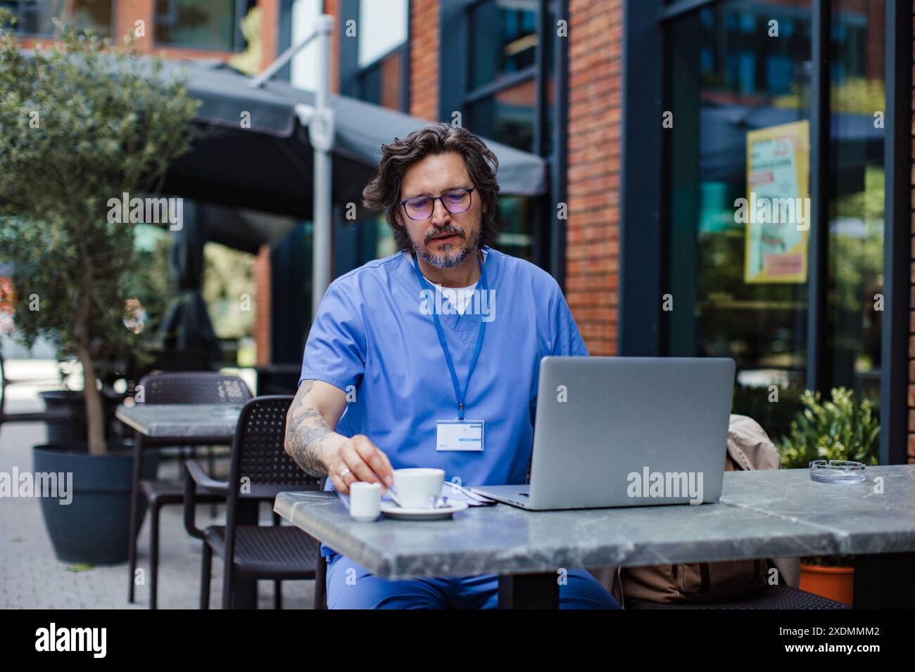 Doctor enjoying cup of coffee in coffee shop, working on laptop ...