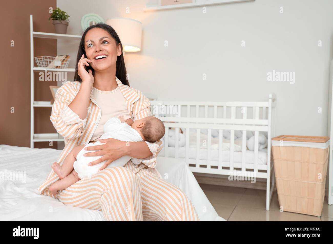 Mother breastfeeding her baby while talking by mobile phone in bedroom ...