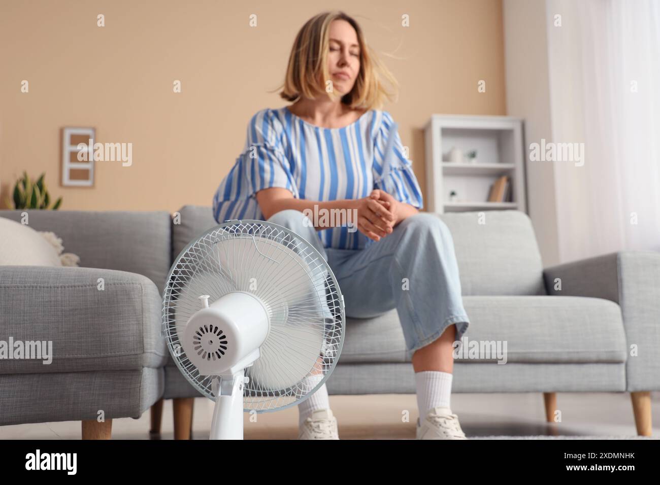 Beautiful mature woman with electric fan sitting on sofa at home Stock ...