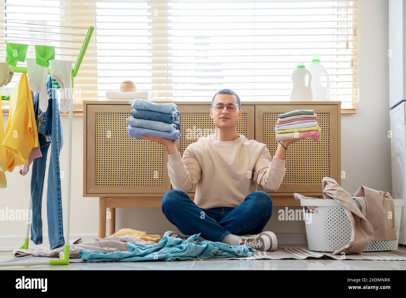 Young man meditating with stacks of clean clothes in laundry room Stock ...
