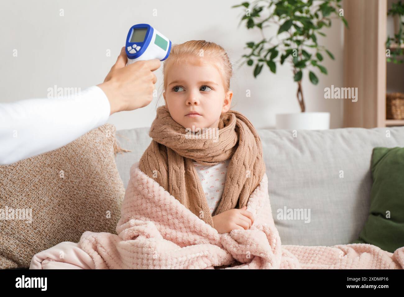 Sick little girl and her mother with infrared thermometer measuring temperature at home Stock ...