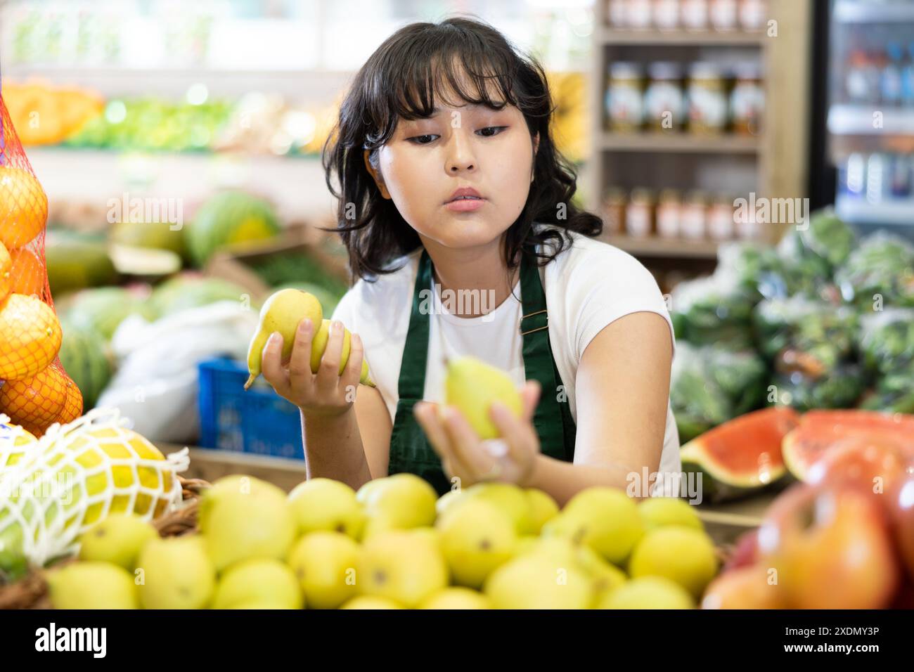 Asian female grocery store worker lays out ripe pears on counter and ...
