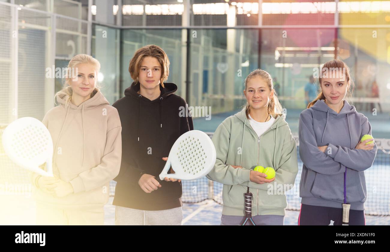 Four paddle tennis players standing on court holding rackets and balls ...