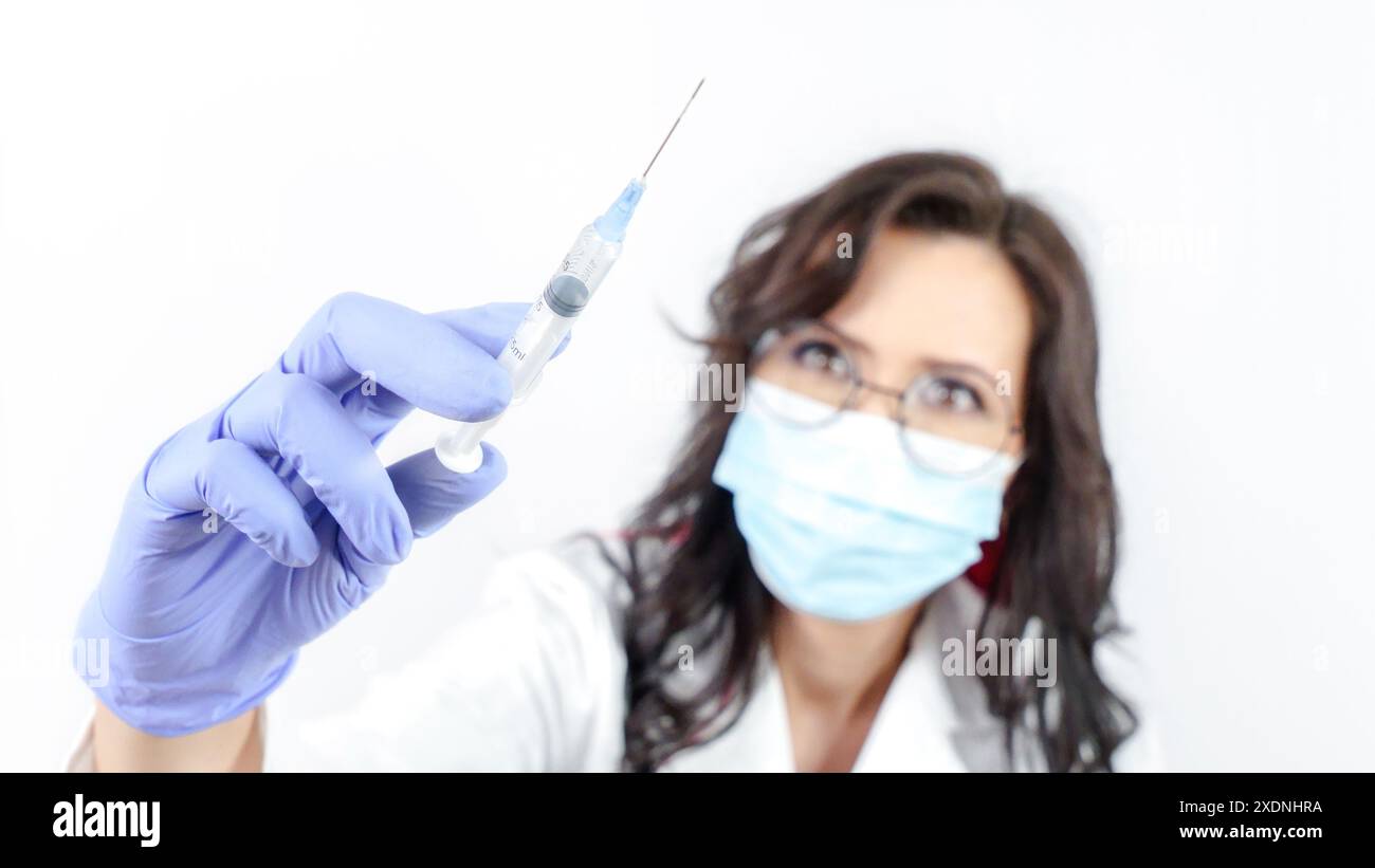 Nurse in blue face mask holding a syringe with a needle isolated on ...