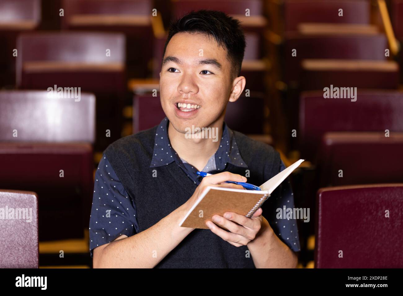 A college student is seated in a lecture hall holding a notebook and ...
