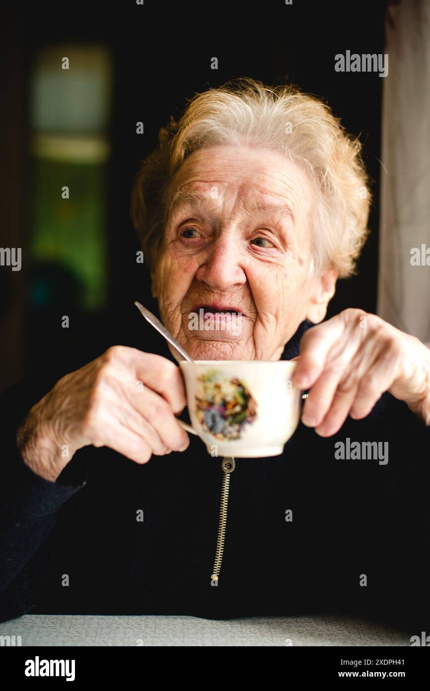 An elderly woman enjoys a cup of tea, savoring a peaceful and ...