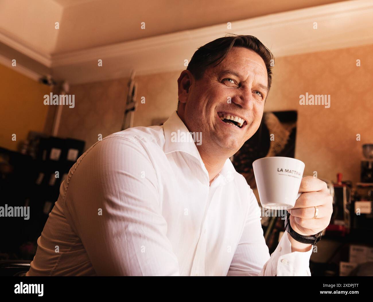 Man in white shirt laughing while drinking coffee in a stylish cafe ...