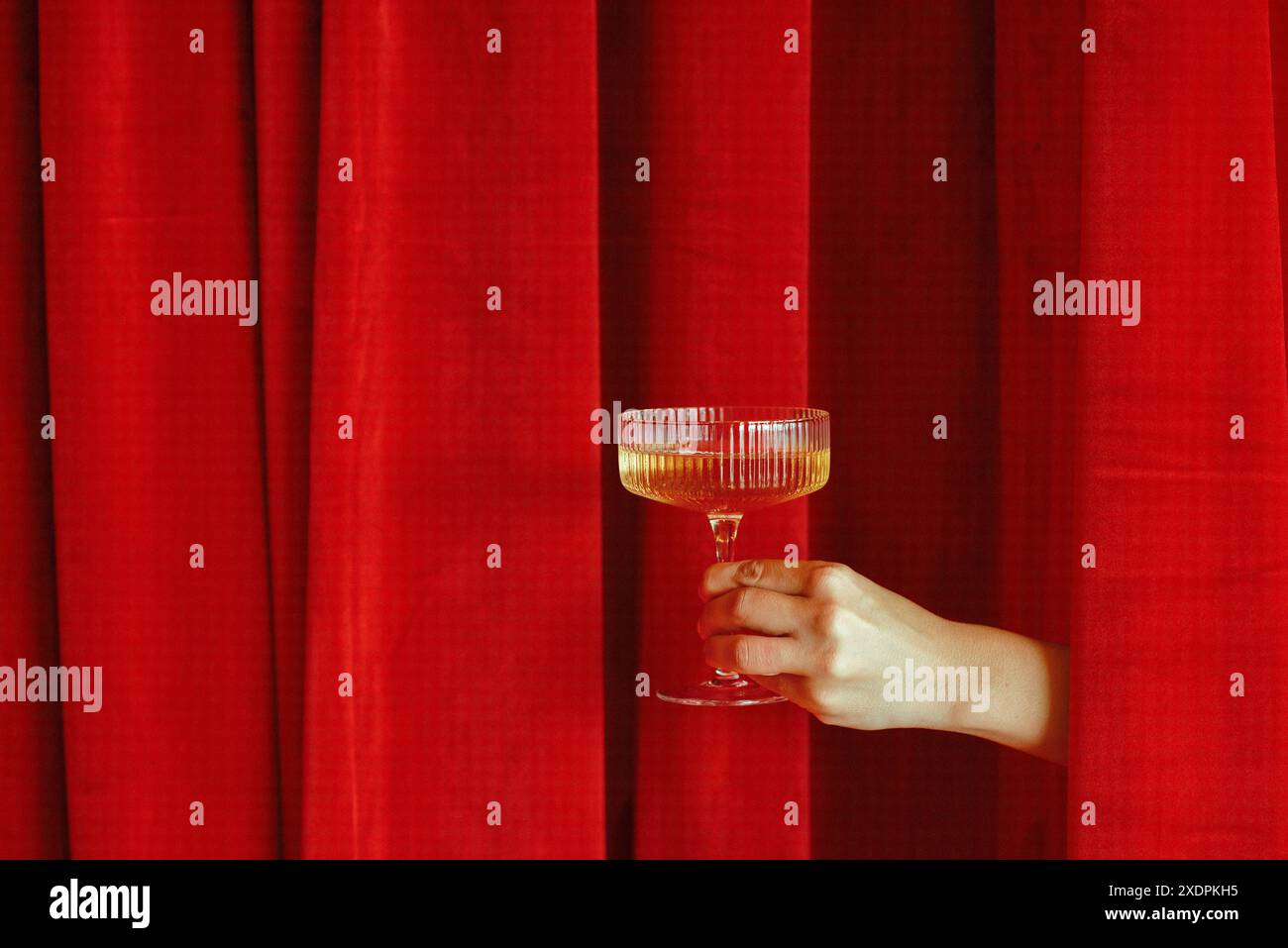 Hand holding a champagne against red velvet curtains Stock Photo - Alamy
