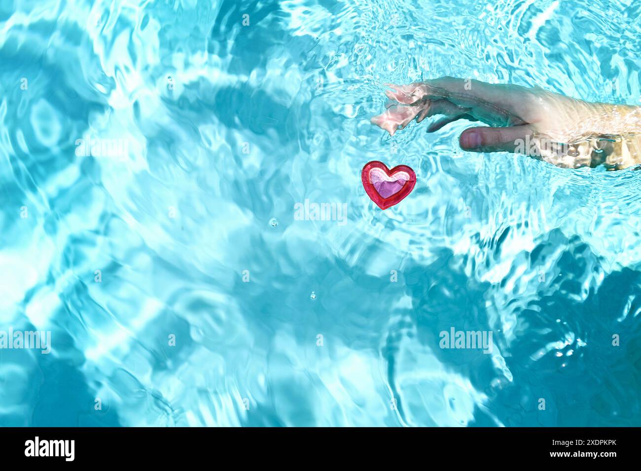Hand near a red heart-shaped object floating in clear blue water Stock ...