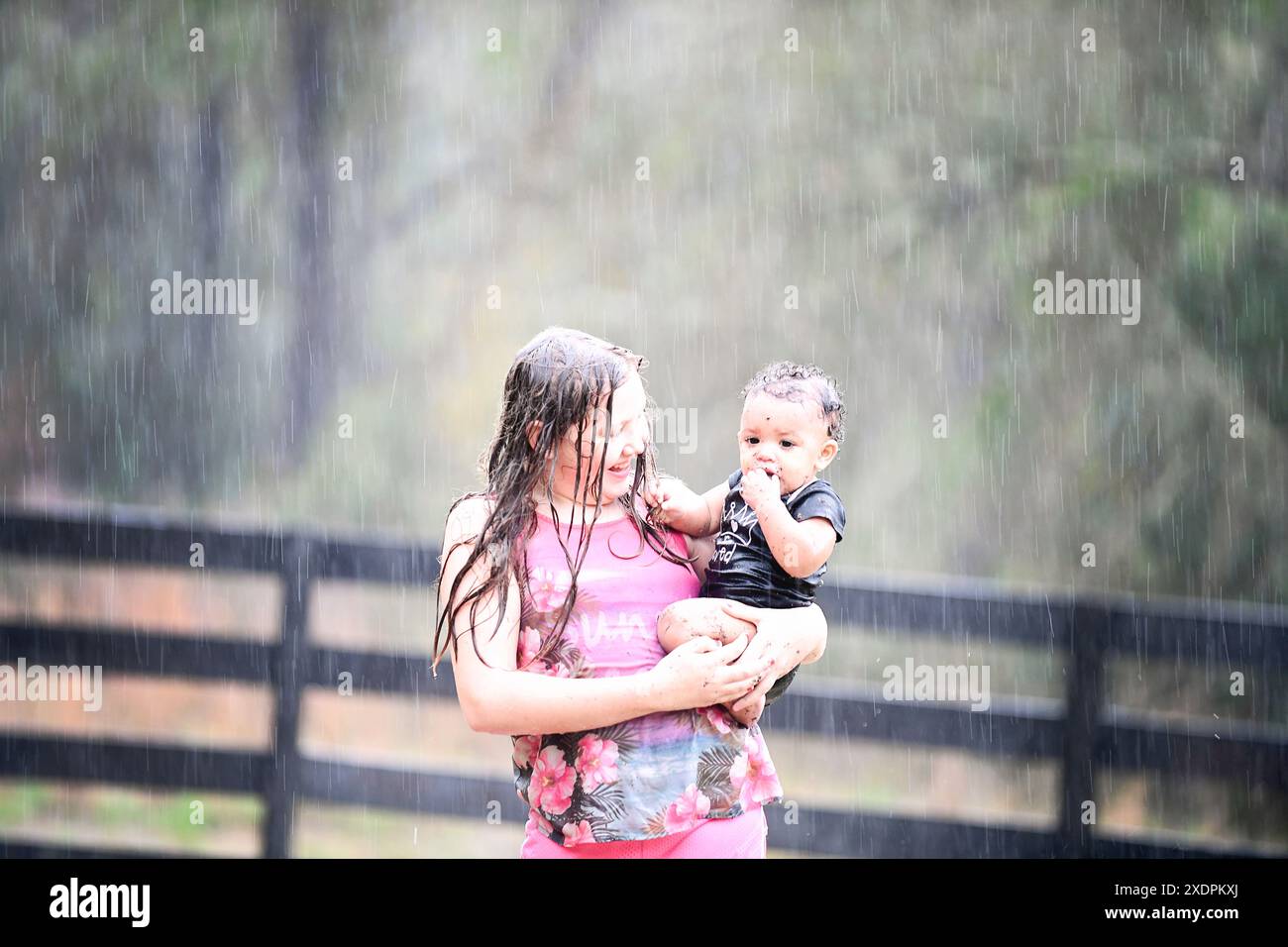 Girl holding a baby in the rain, both smiling and wet Stock Photo - Alamy