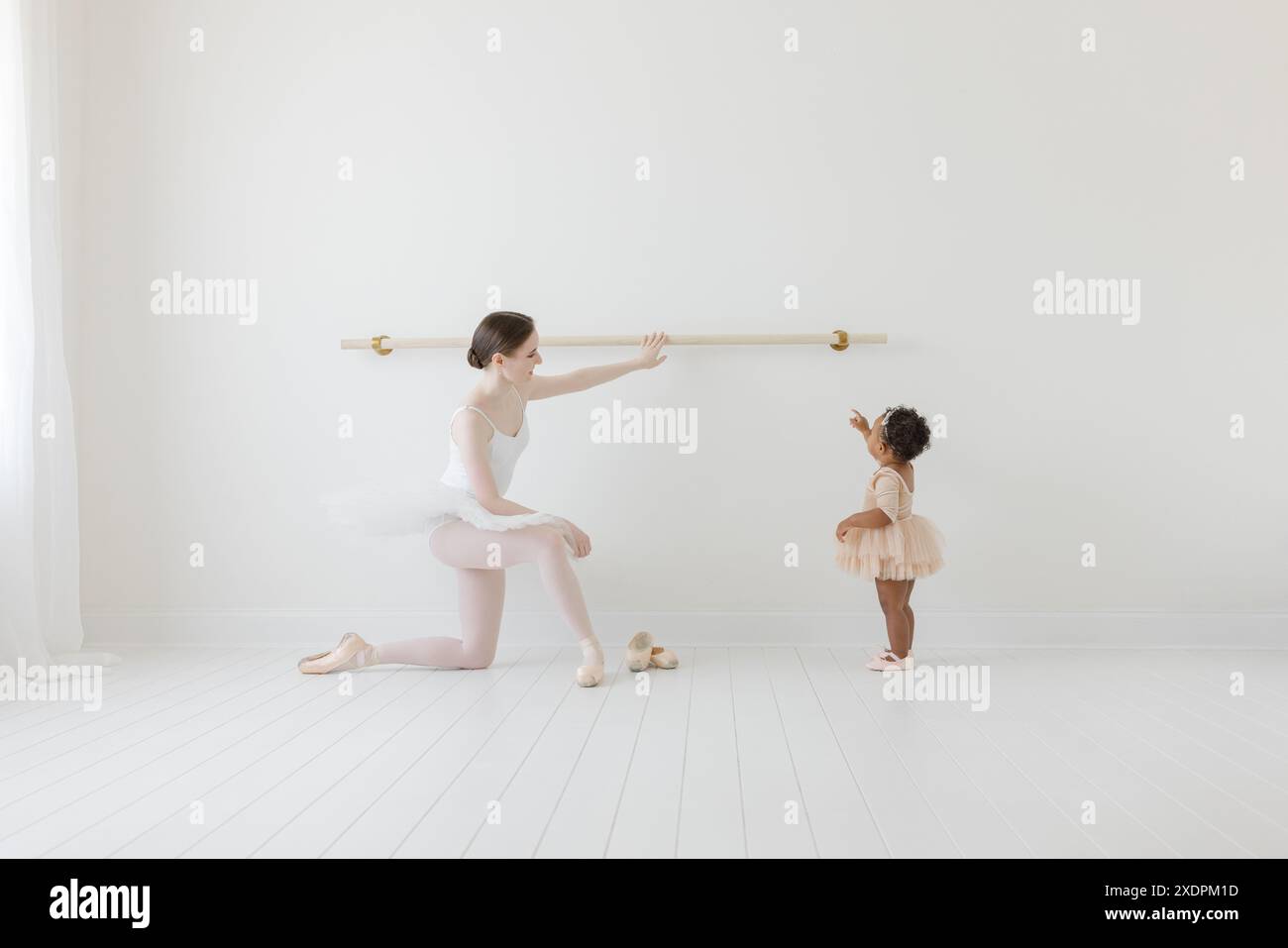 Adult Ballerina shows BIPOC baby ballet barre in white studio Stock ...