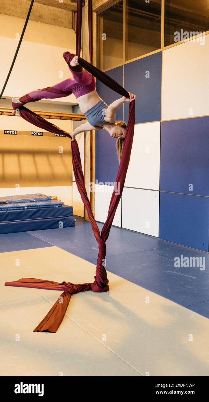 Woman performing an inverted acrobatic routine on aerial silks in a ...