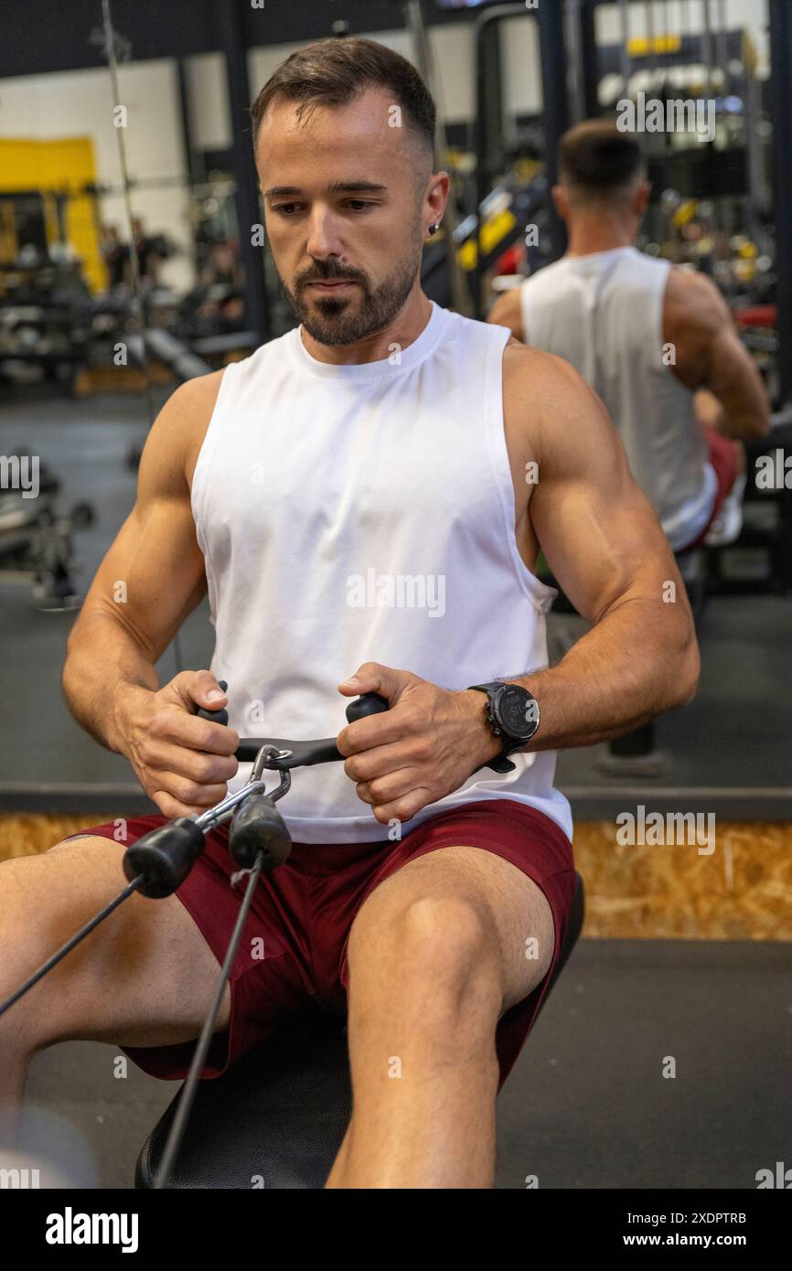 Muscular man in the gym training back sitting on the bench Stock Photo ...