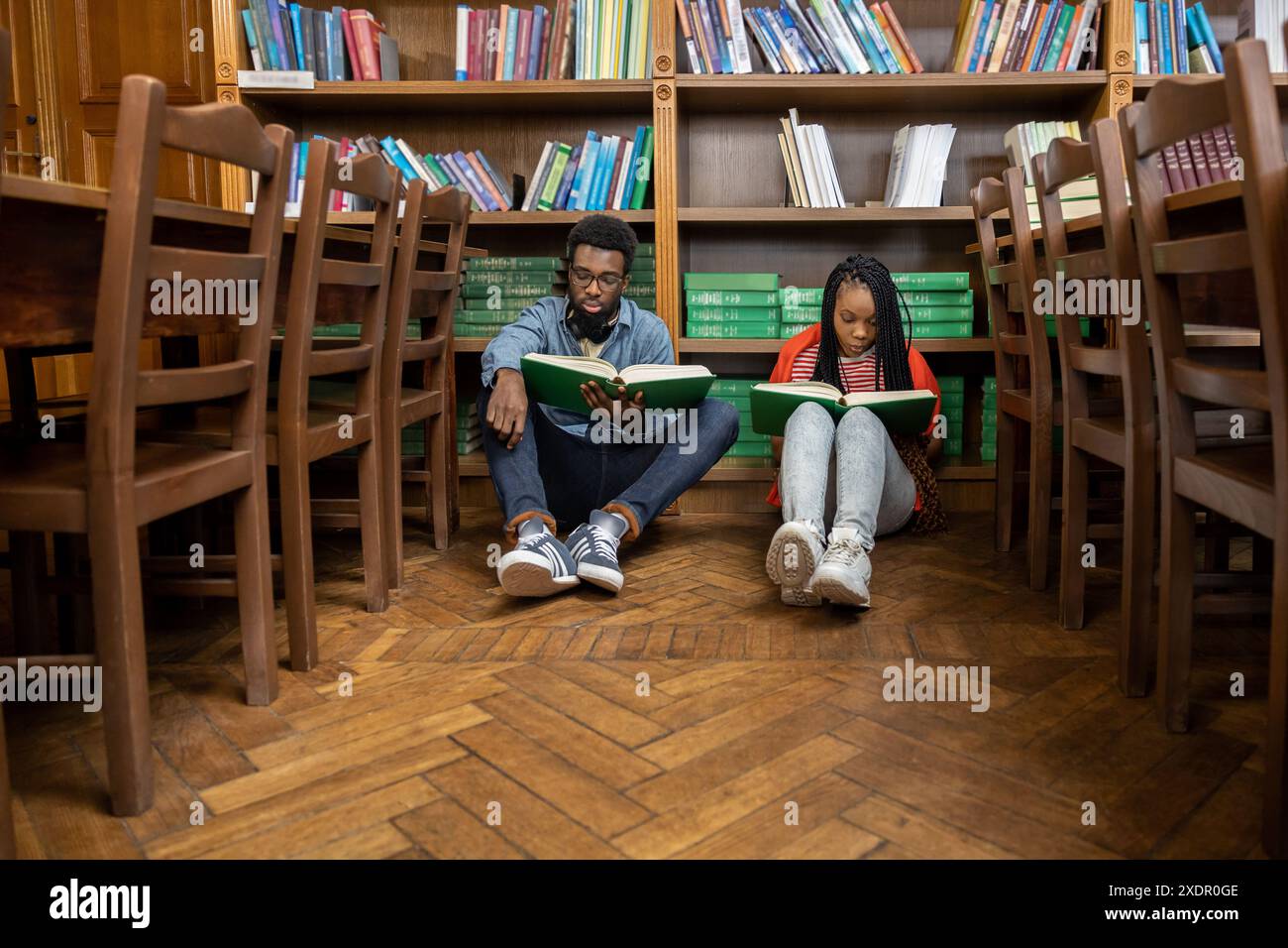 Two young people sitting on the floor in the library and reading a book ...