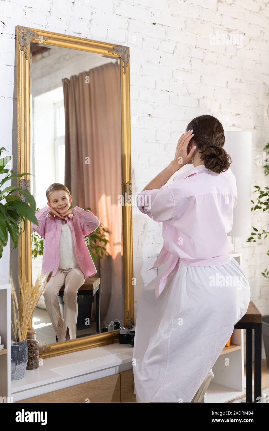 Continuity. Young lady looks into mirror, where little child, girl in ...