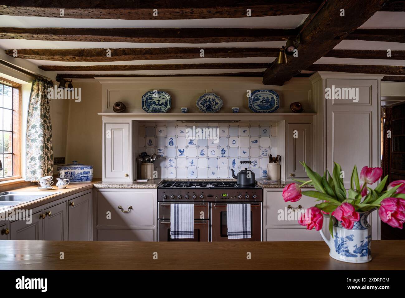Pink tulips and kettle on hob with Delft tiles in beamed kitchen of ...